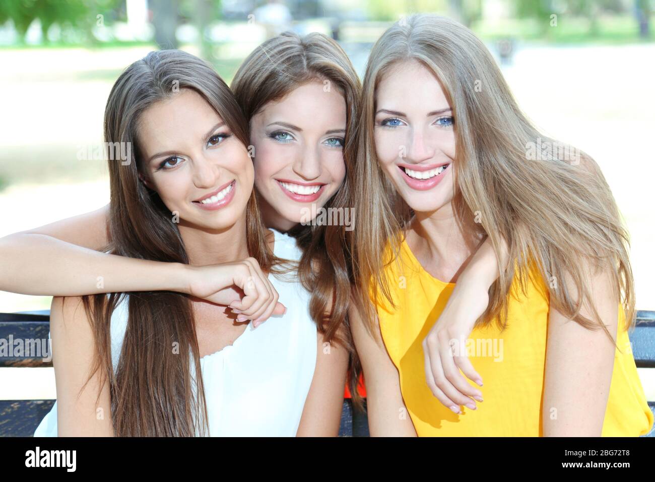 Three beautiful young woman sitting on bench in summer park Stock Photo ...