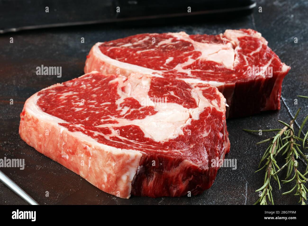 Two fresh raw rib-eye steak with rosmary in a rustic style background ...
