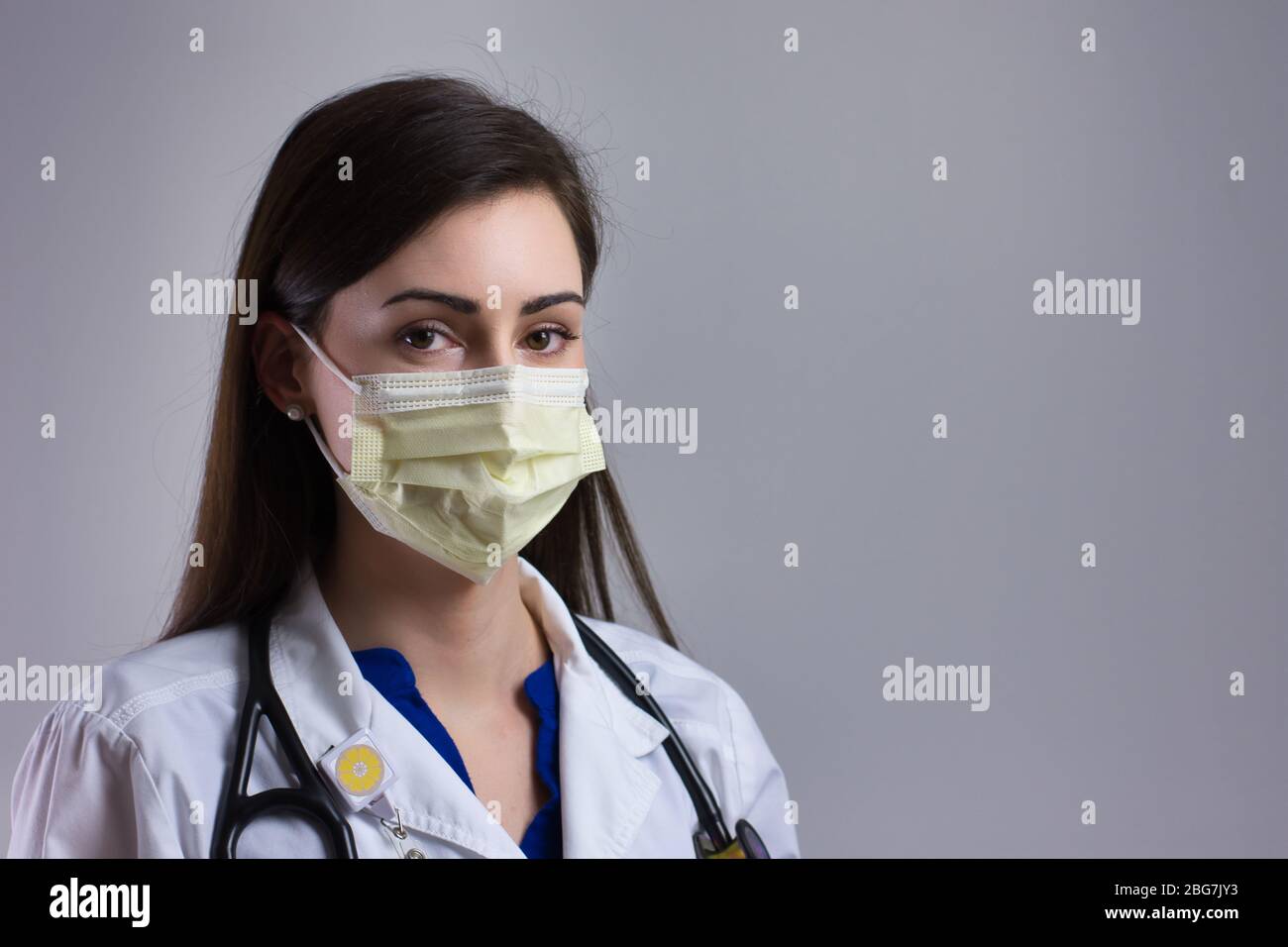 Masked healthcare worker smiling and posing under yellow mask against a ...