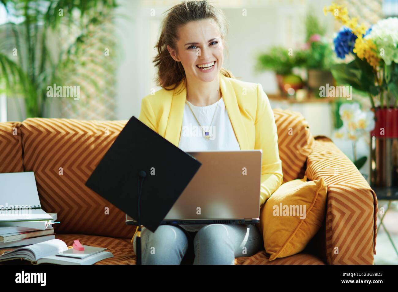 smiling modern student in jeans and yellow jacket with graduation cap ...