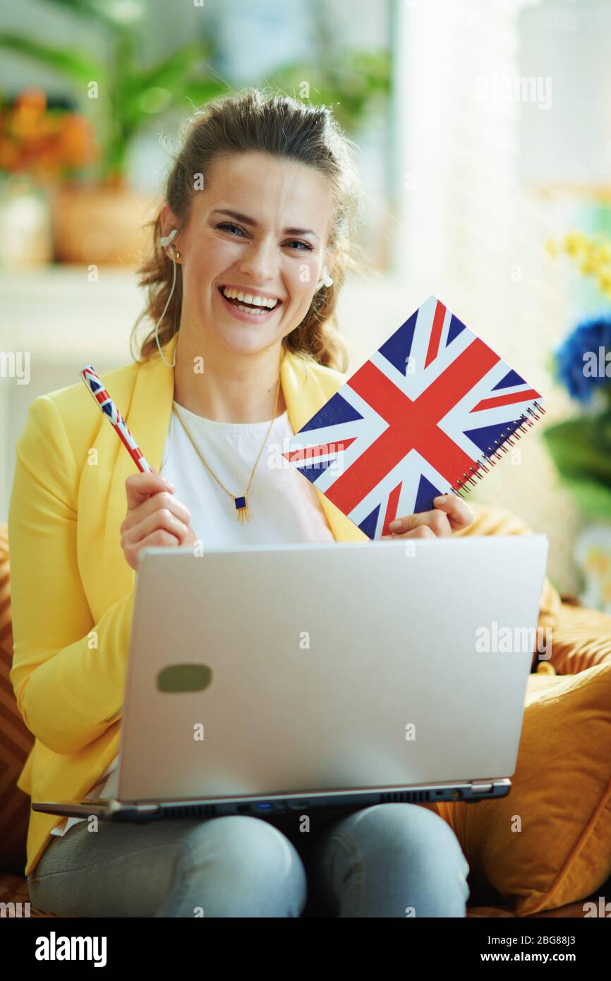 smiling 40 years old woman in jeans and yellow jacket with laptop ...