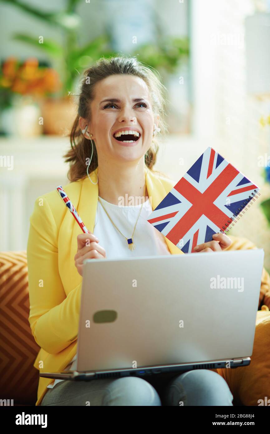 happy elegant middle age woman in jeans and yellow jacket with laptop ...