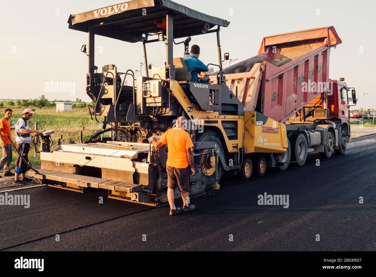 road construction workers operating pavement machine laying a fresh ...