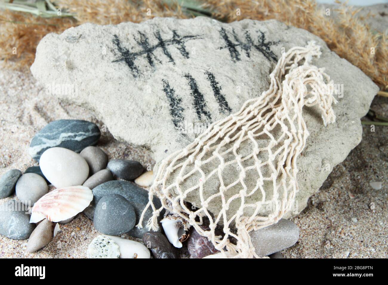 Counting days by drawing sticks on stone with stones and shells on sand ...