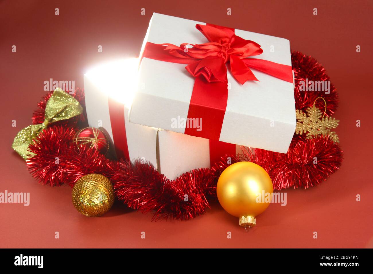 Gift box with bright light on it on red background Stock Photo - Alamy