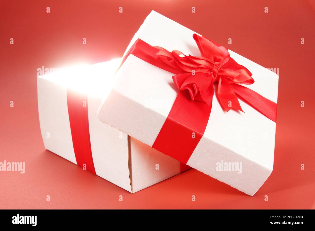 Gift box with bright light on it on red background Stock Photo - Alamy
