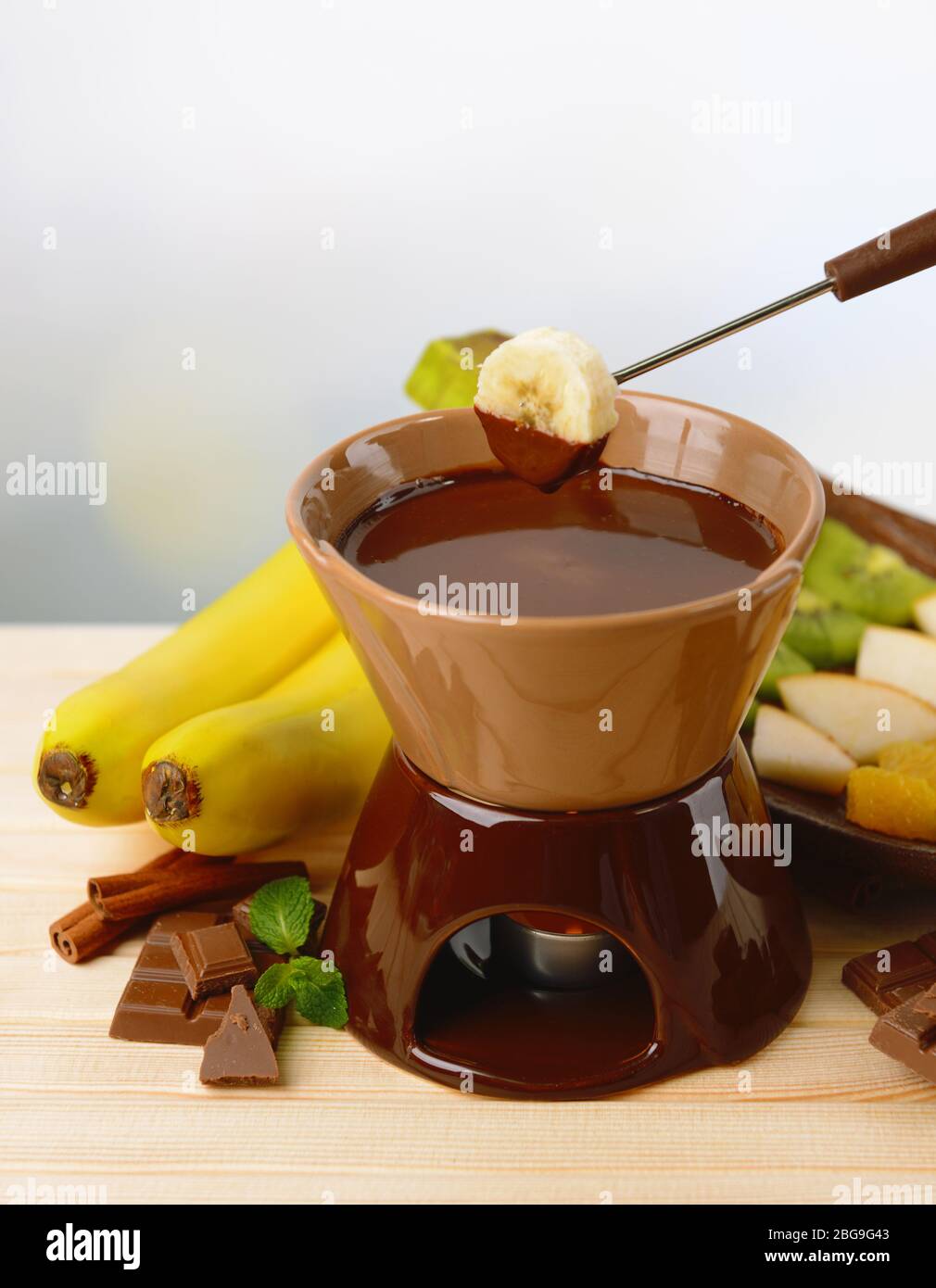 Chocolate fondue with fruits, on wooden table, on light background ...