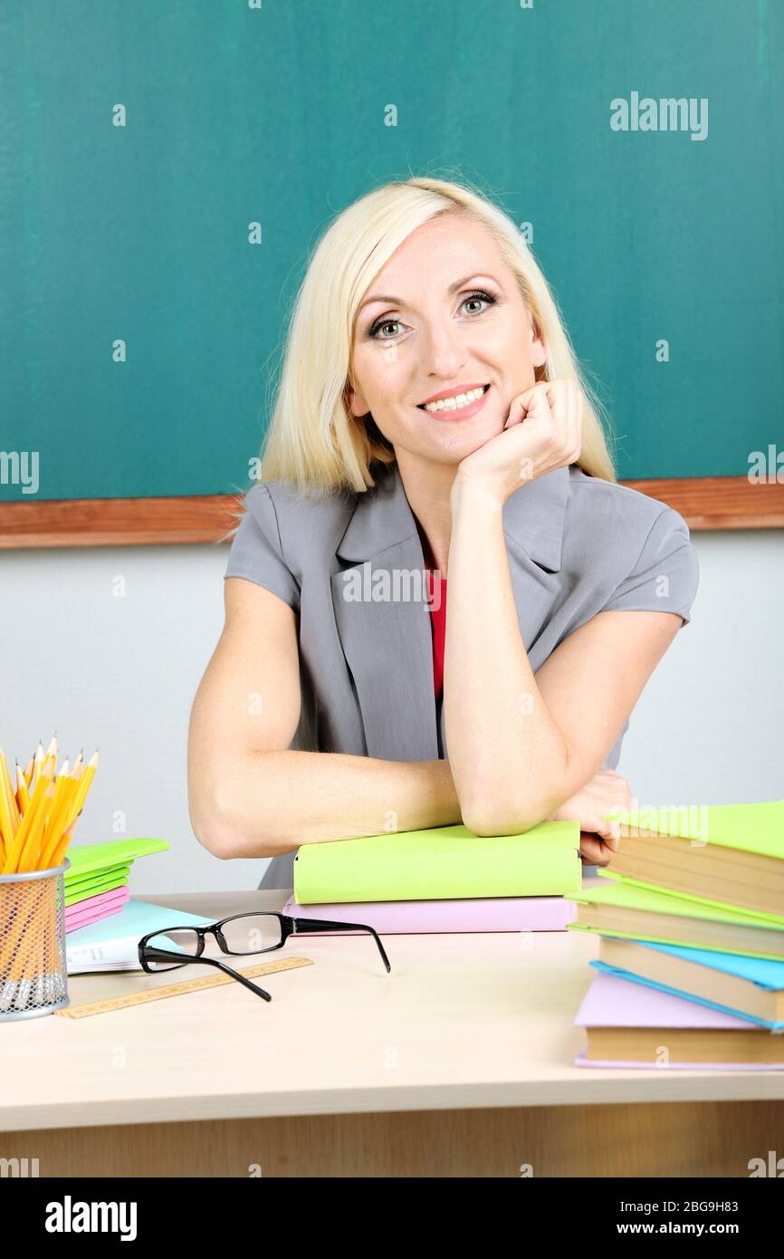 School teacher sitting at table on blackboard background Stock Photo ...