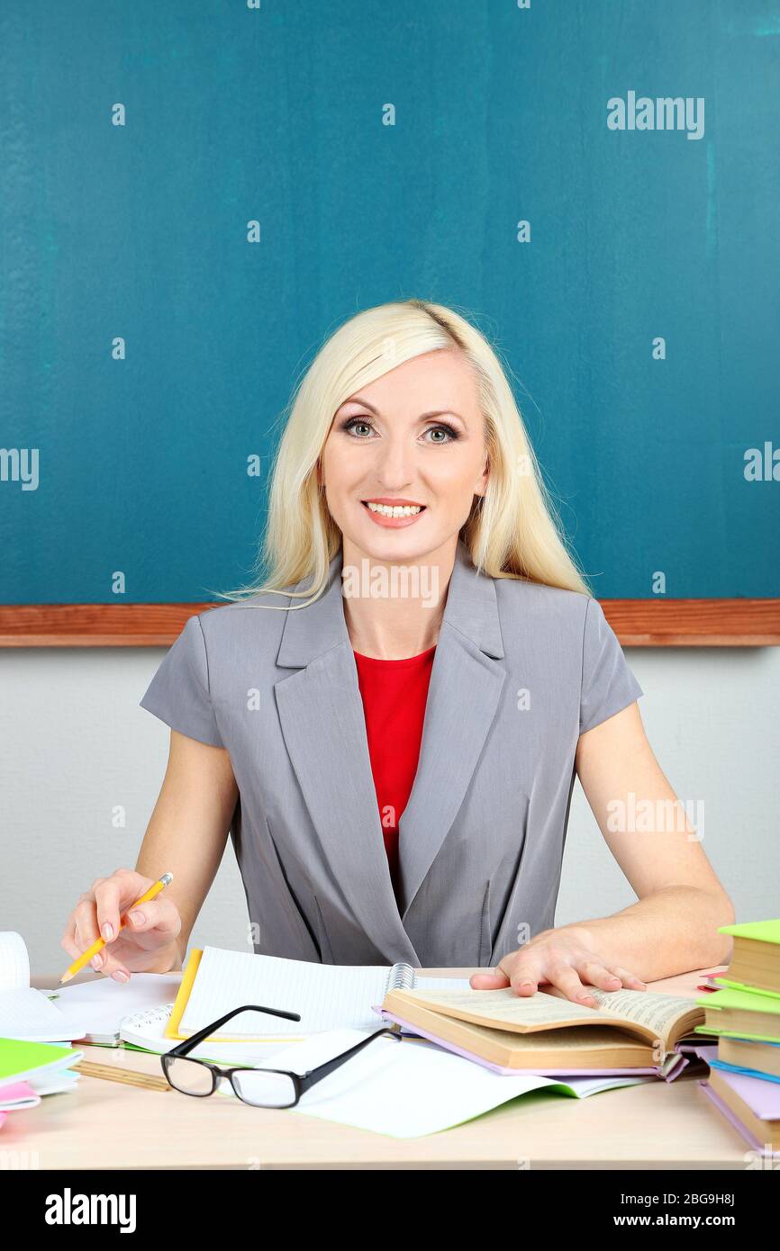 School teacher sitting at table on blackboard background Stock Photo ...