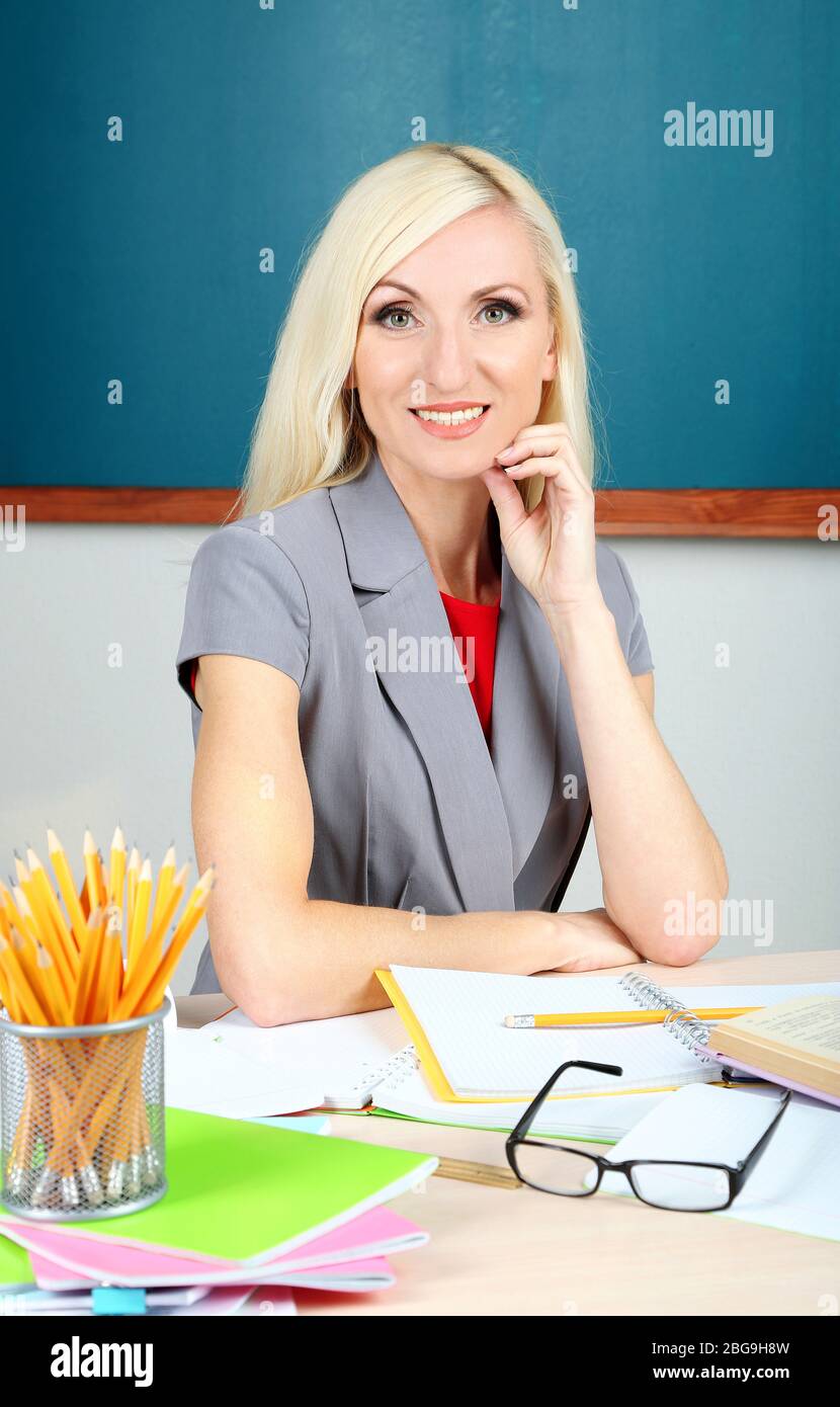 School teacher sitting at table on blackboard background Stock Photo ...