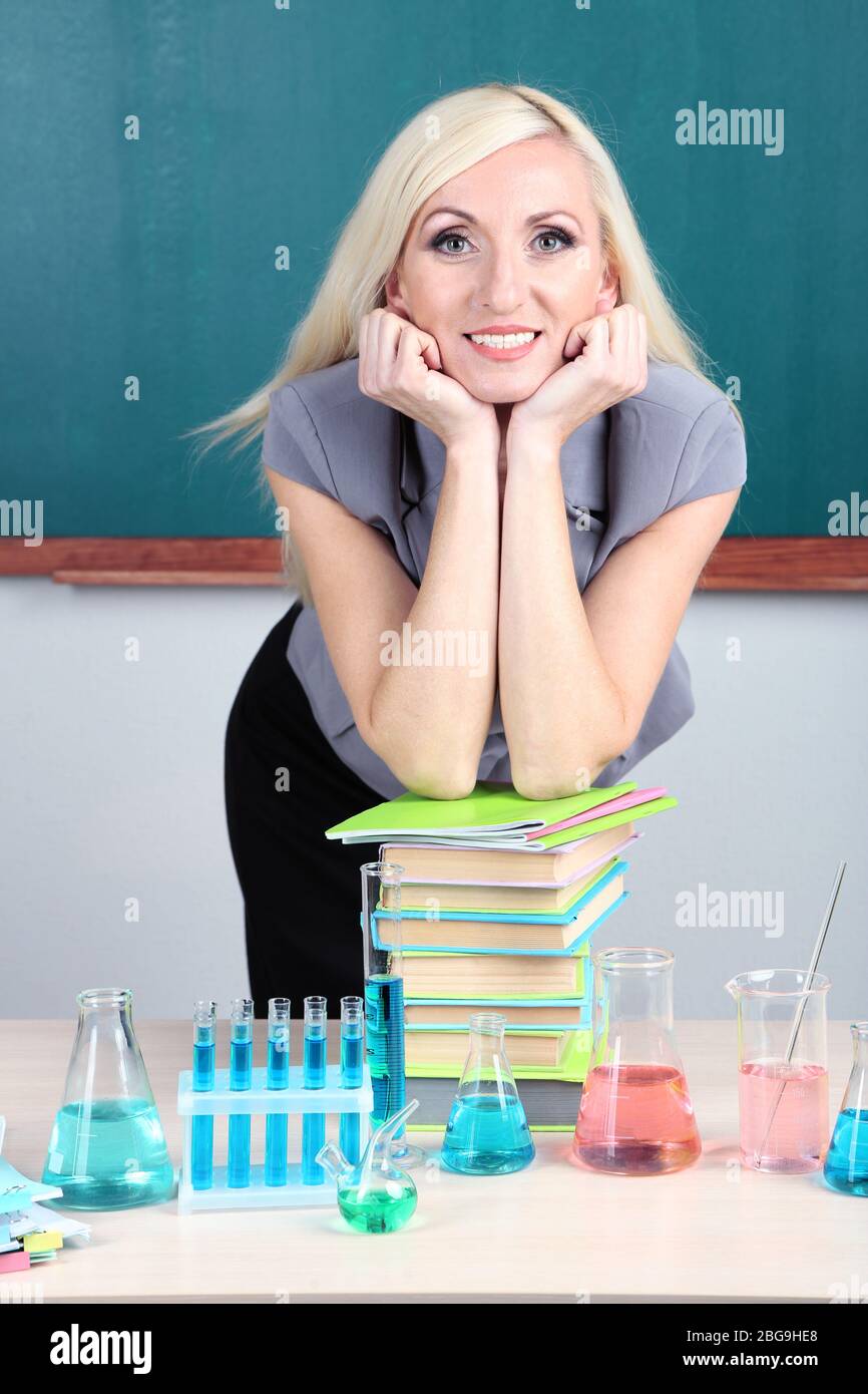 Chemistry teacher standing near table with tubes on blackboard ...