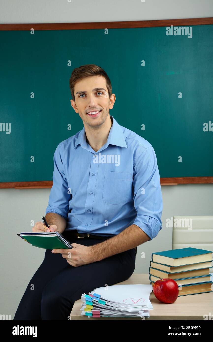 Young teacher sitting on desk in school classroom Stock Photo - Alamy