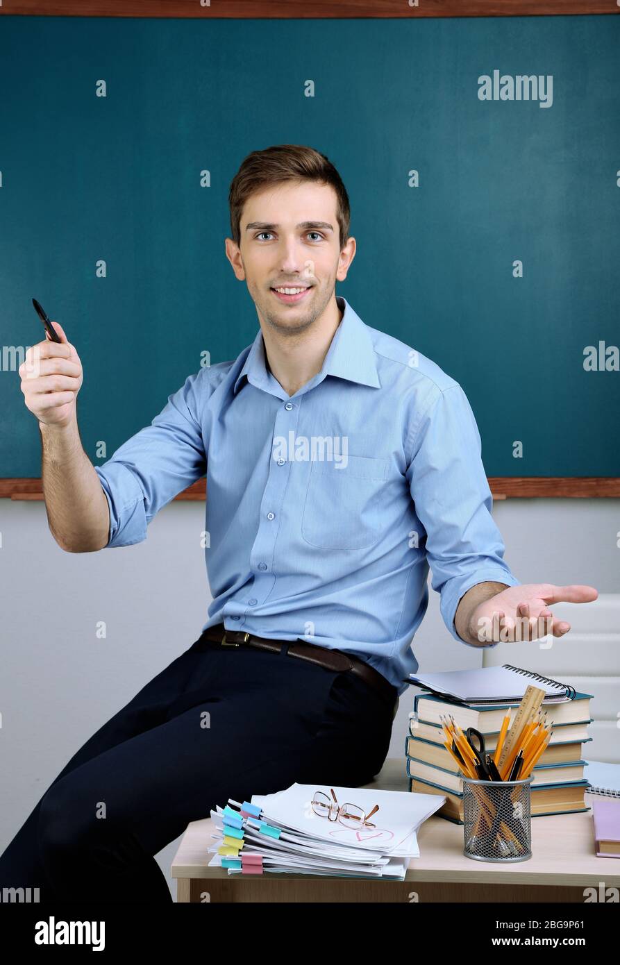 Young teacher sitting on desk in school classroom Stock Photo - Alamy