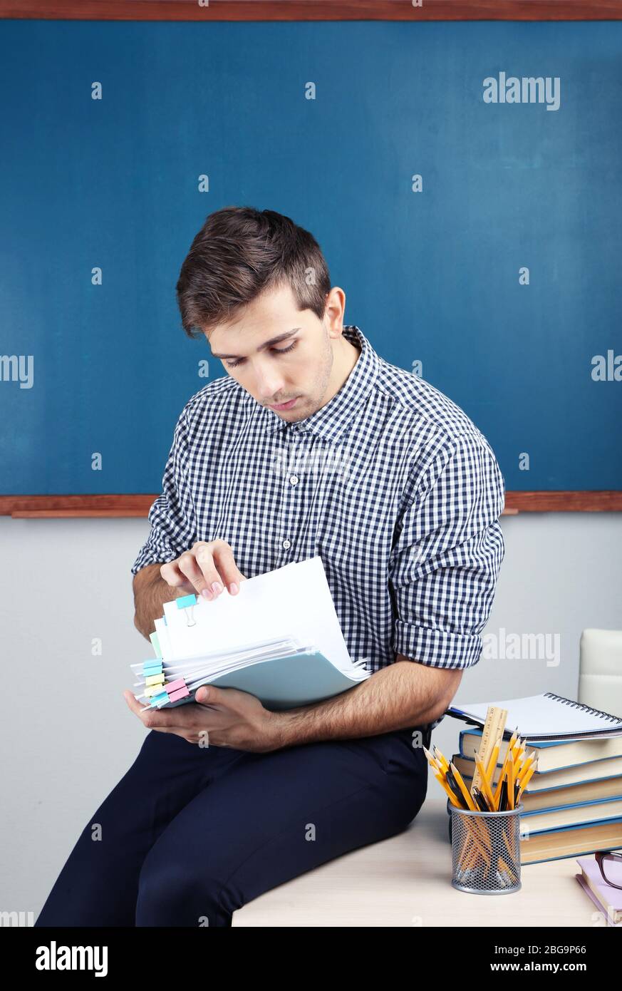 Young teacher sitting on desk in school classroom Stock Photo - Alamy