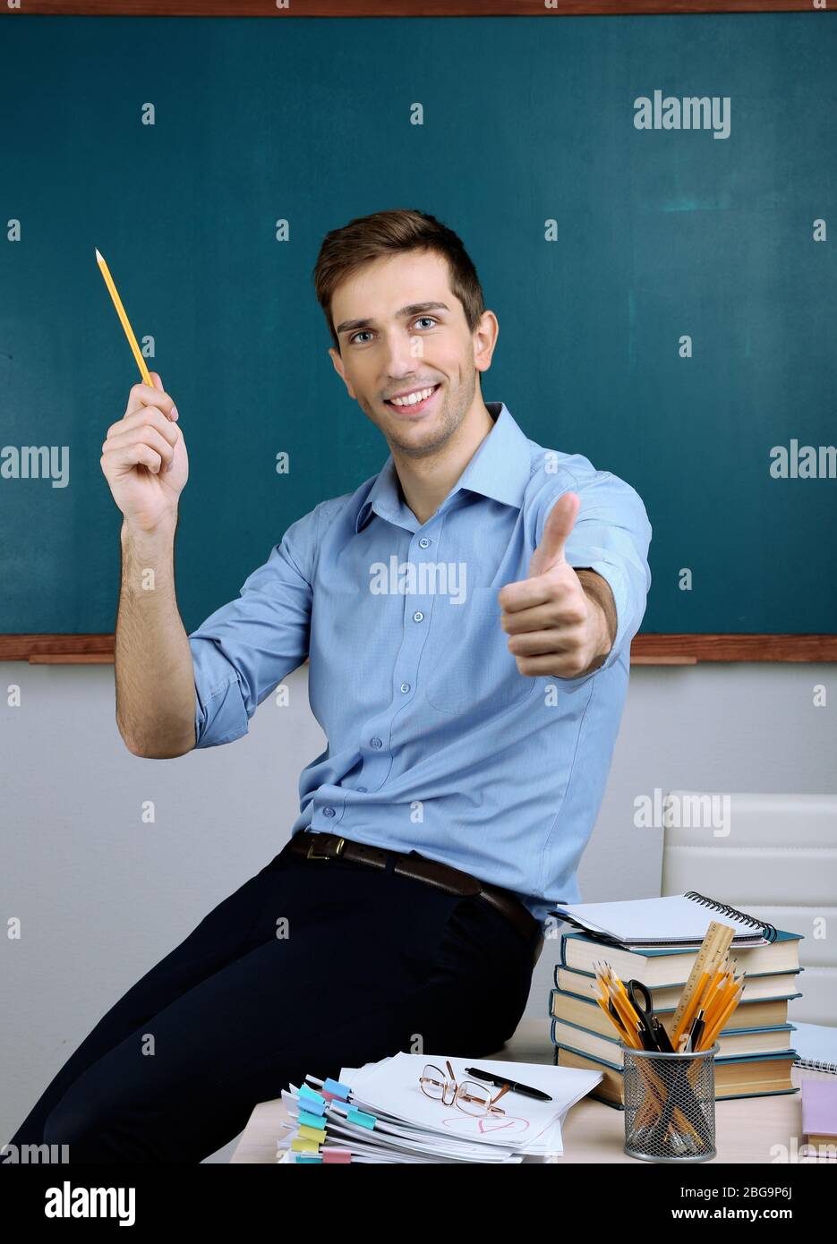 Young teacher sitting on desk in school classroom Stock Photo - Alamy