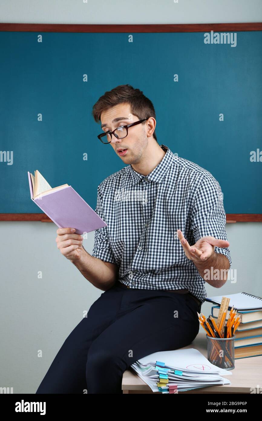 Young teacher sitting on desk in school classroom Stock Photo - Alamy