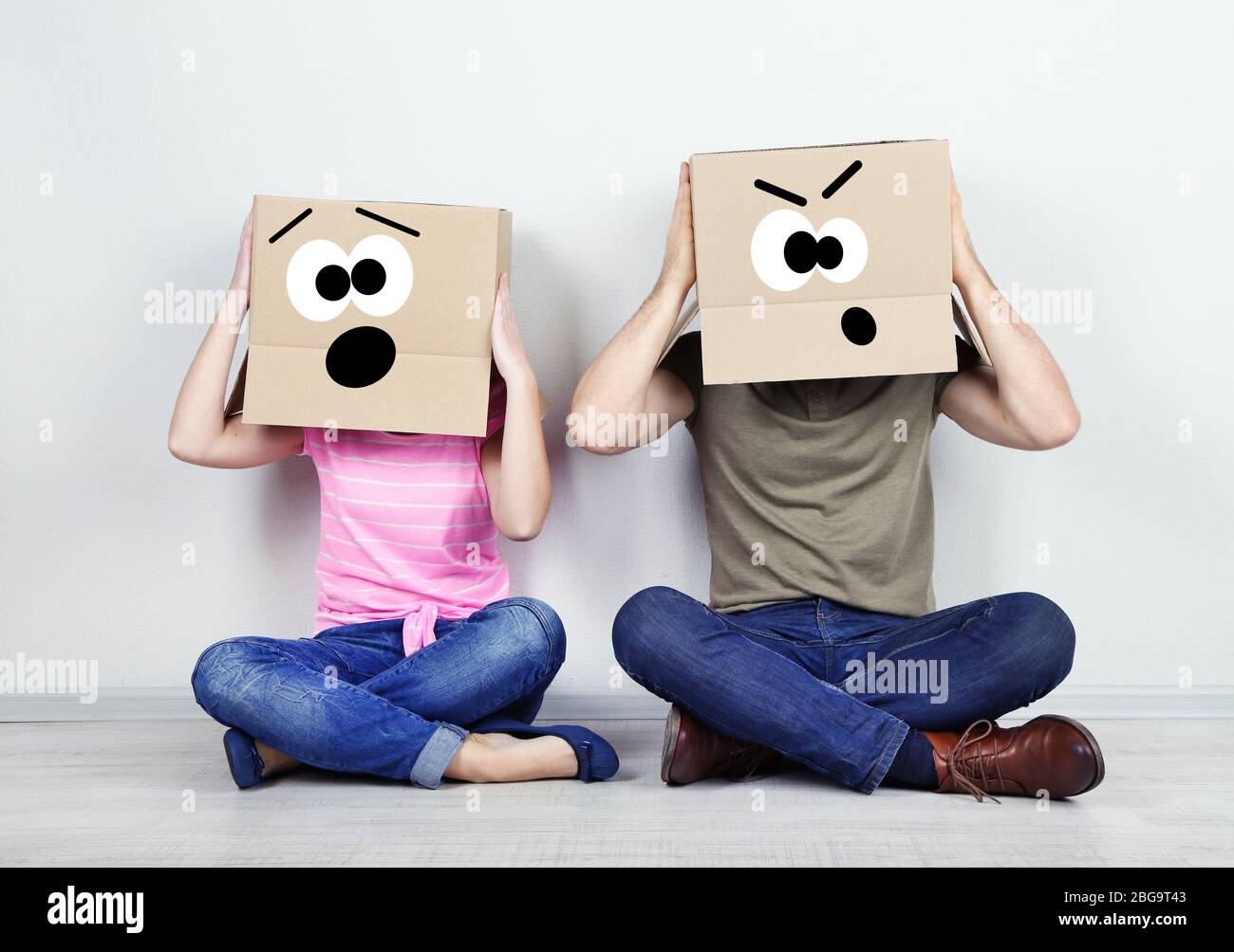 Couple with cardboard boxes on their heads sitting on floor near wall ...