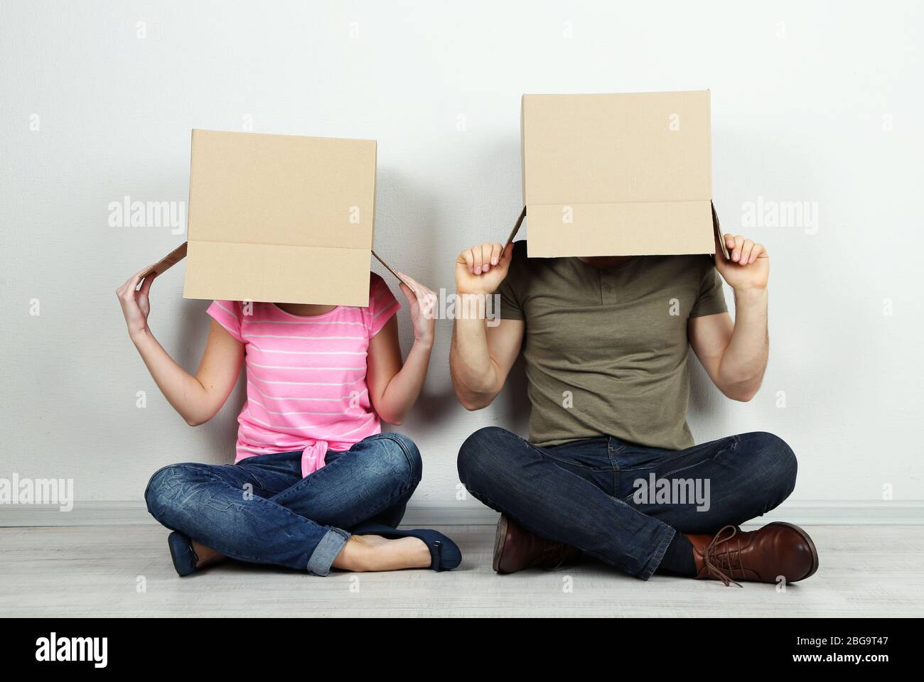Couple with cardboard boxes on their heads sitting on floor near wall ...