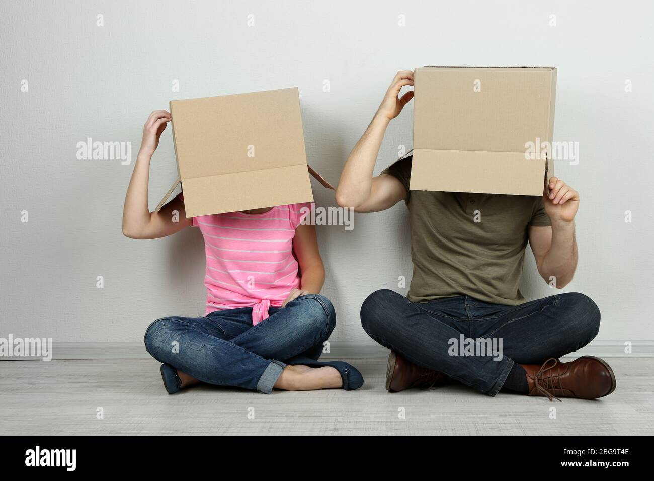 Couple with cardboard boxes on their heads sitting on floor near wall ...