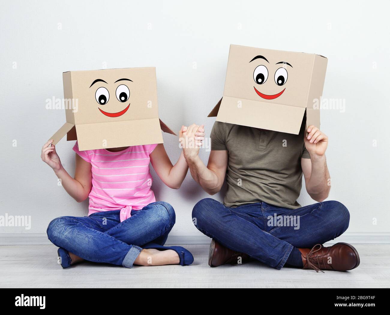 Couple with cardboard boxes on their heads sitting on floor near wall ...