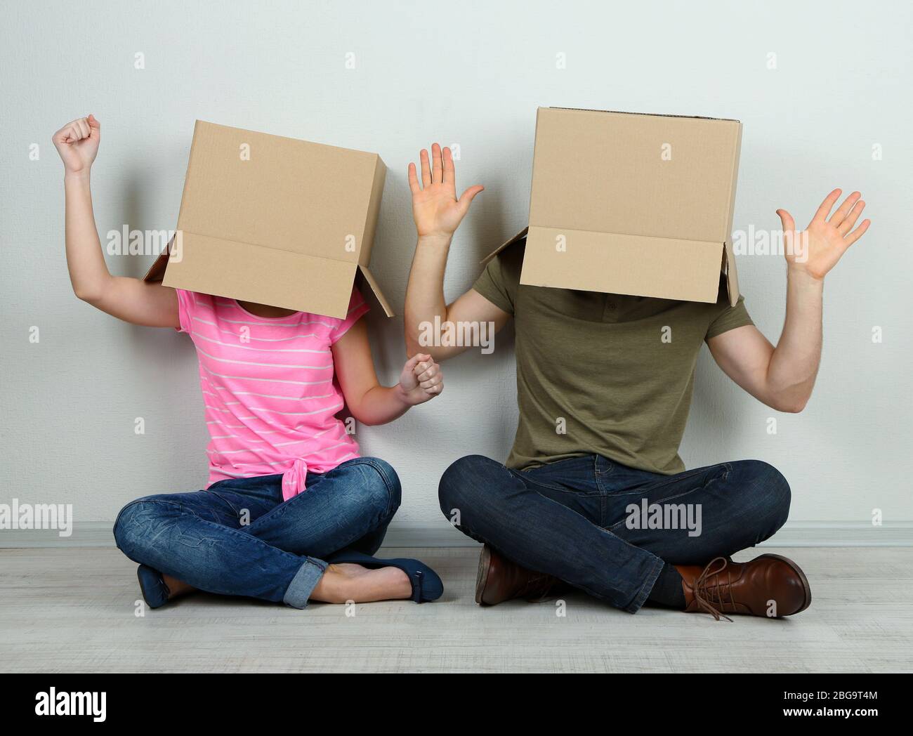 Couple with cardboard boxes on their heads sitting on floor near wall ...