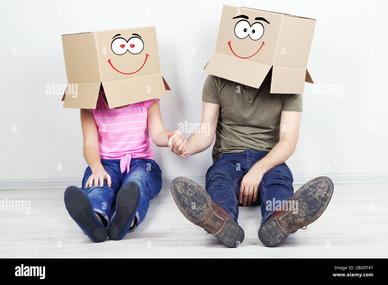 Couple with cardboard boxes on their heads sitting on floor near wall ...