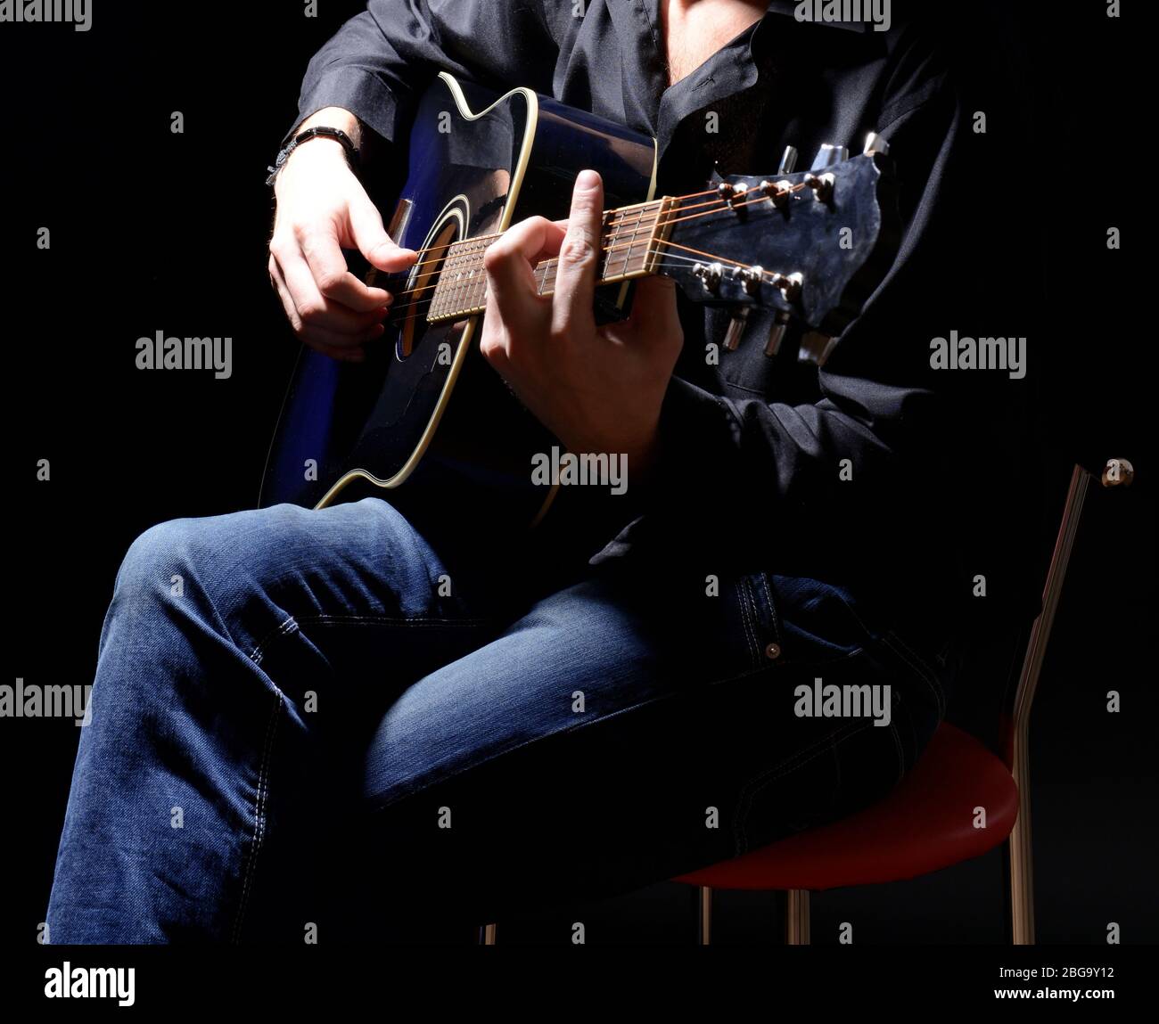 Young musician playing acoustic guitar and singing, on dark background ...