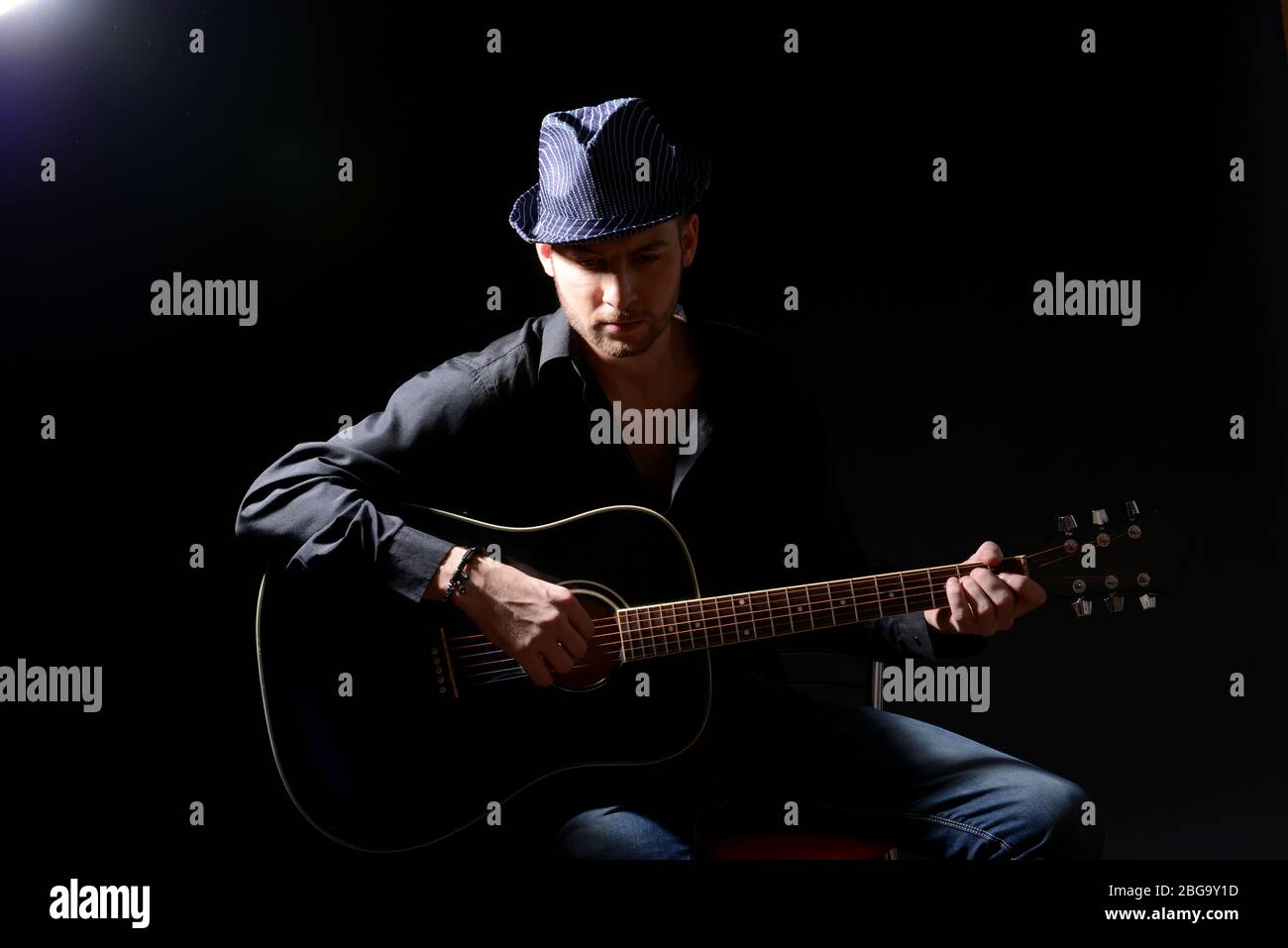 Young musician playing acoustic guitar and singing, on dark background ...