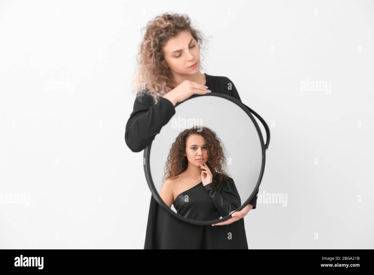 Beautiful model holding mirror with reflection of young woman on white ...