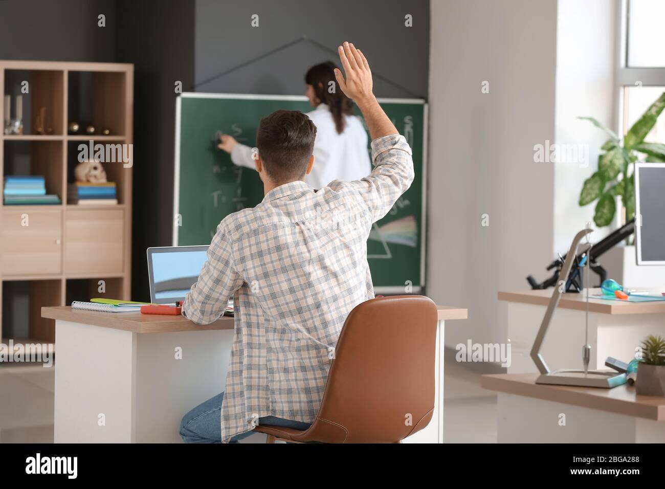Young man with raised hand at physics lesson in classroom Stock Photo ...