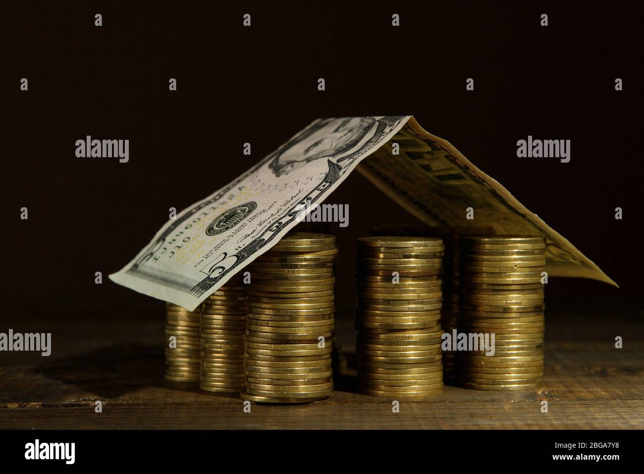 Coins house on table on brown background Stock Photo - Alamy