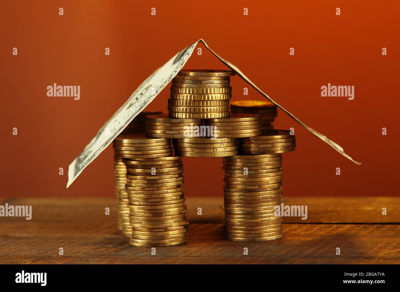 Coins house on table on brown background Stock Photo - Alamy