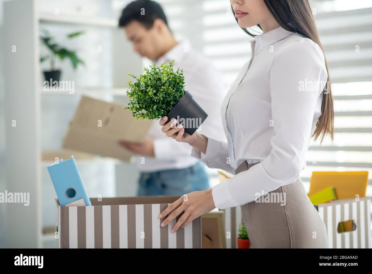 Brunette female standing at her desk, putting her personal stuff into ...
