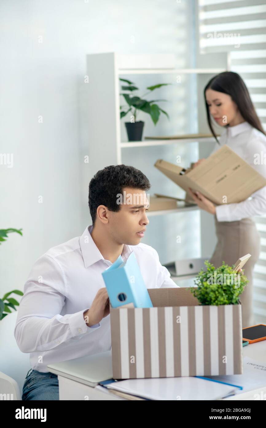 Upset young brunette male sitting at his desk, putting his personal ...