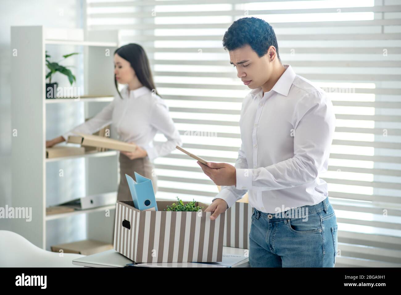 Upset young brunette male packing his personal stuff into box, his ...