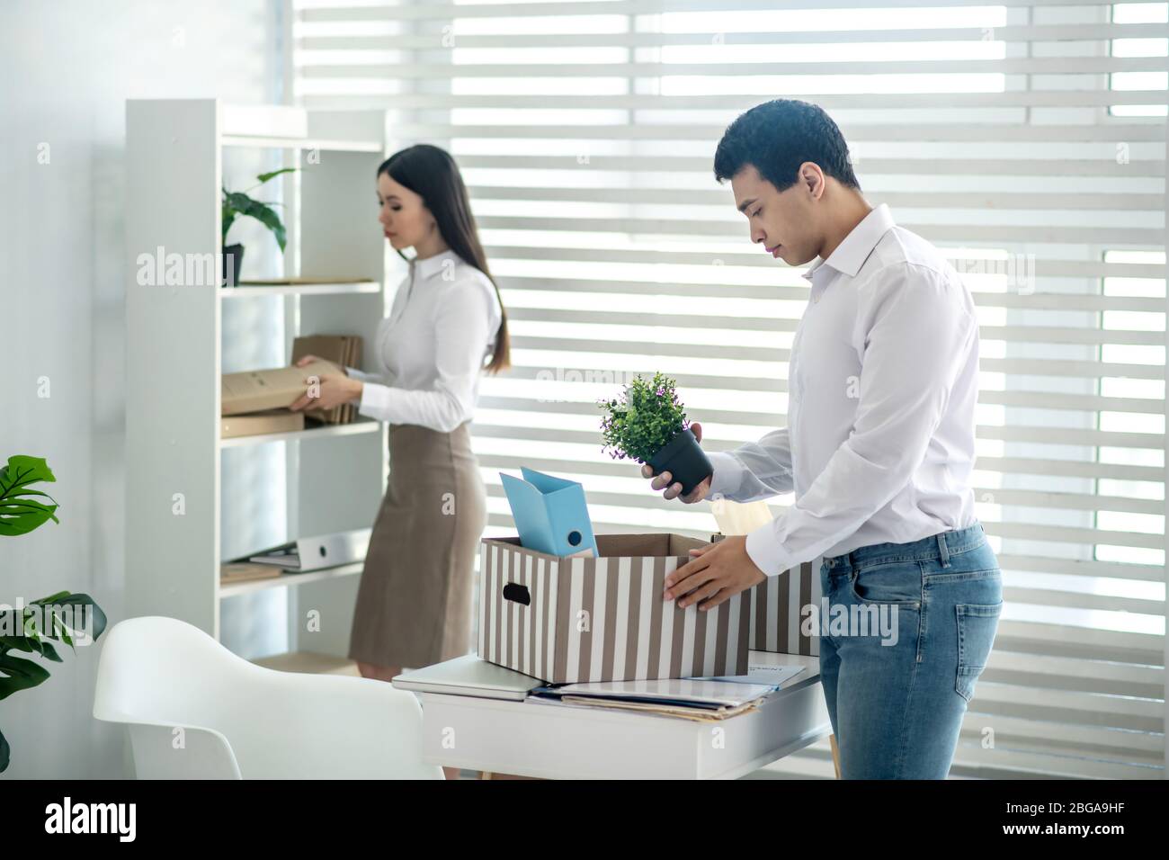 Upset young brunette male personal stuff into box Stock Photo - Alamy