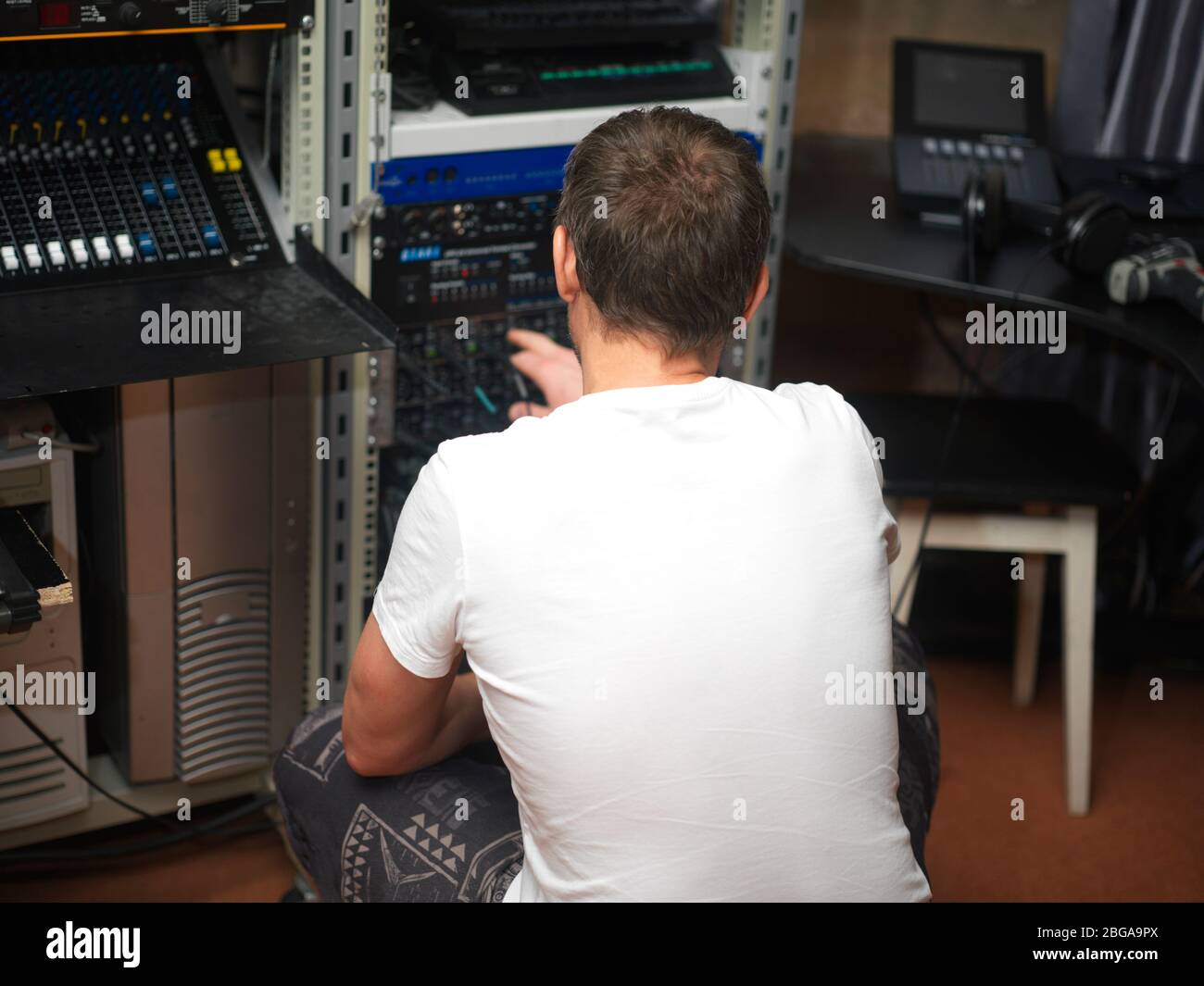A sound engineer sitting in front of rack mounted musical equipment ...