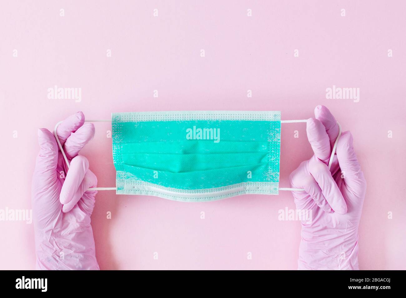 Hands in pink surgical latex gloves holding green surgical mask on pink ...