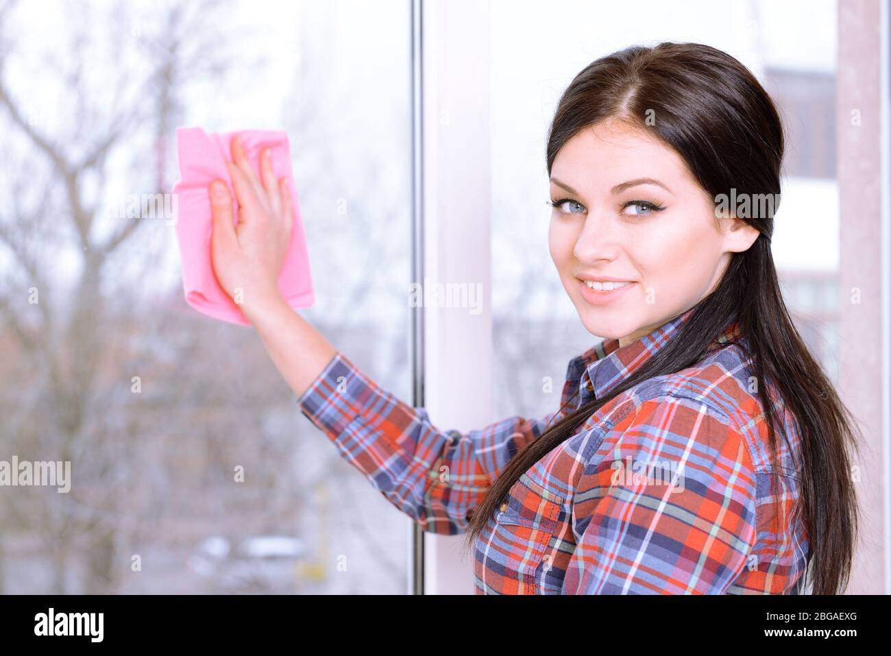 Beautiful young woman washing window in room Stock Photo - Alamy