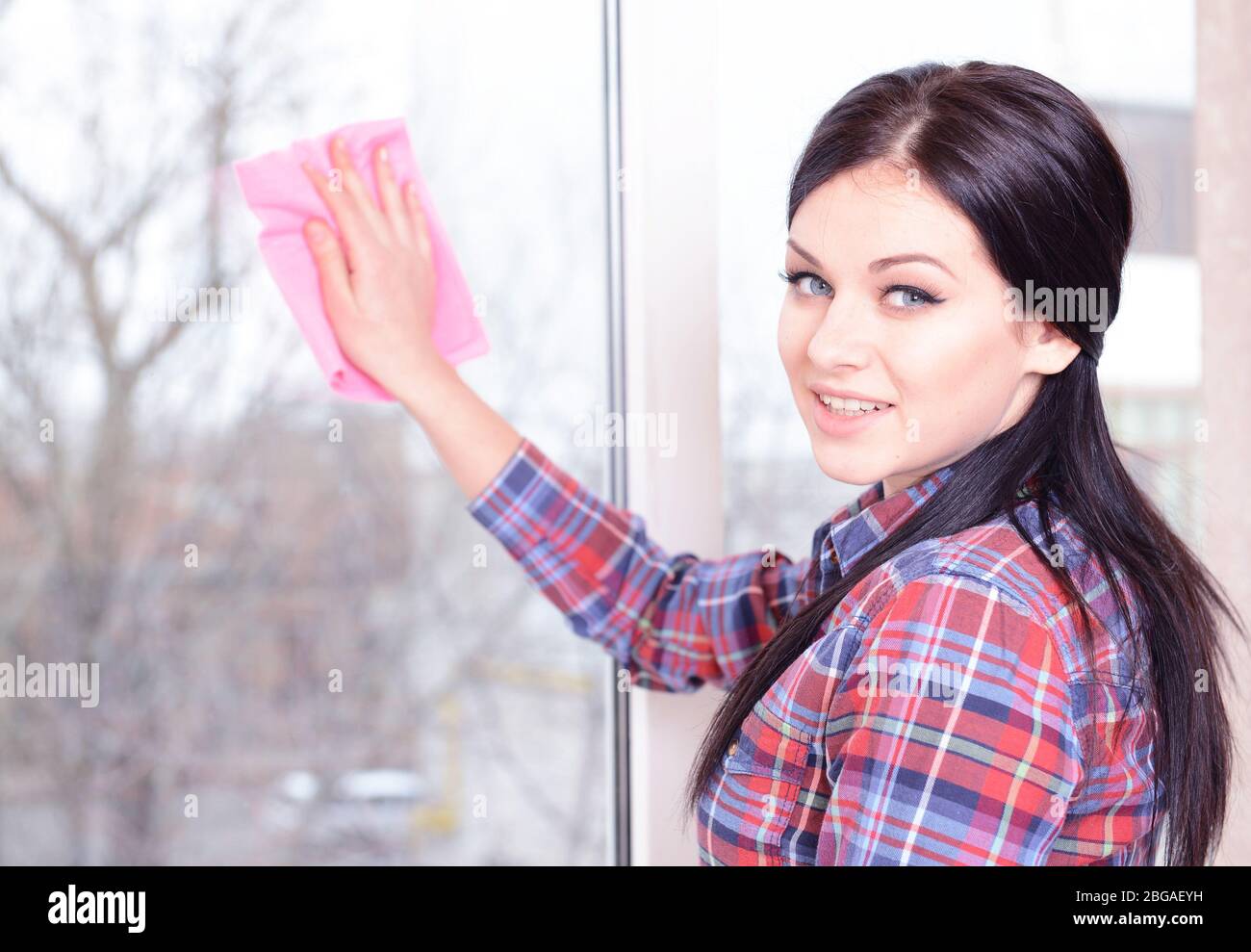 Beautiful young woman washing window in room Stock Photo - Alamy