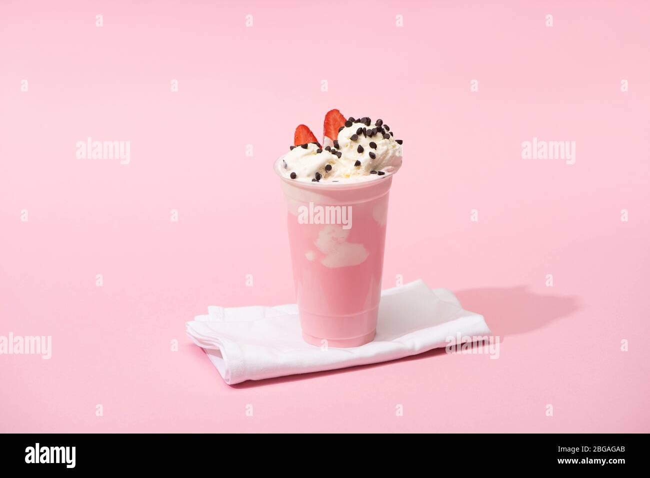 Disposable cup of milkshake with chocolate chips and strawberry halves ...
