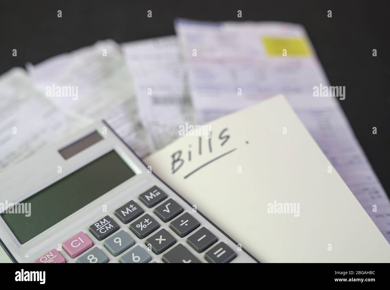 Calculator on top of notepad with the words Bills. Stack of bills at ...