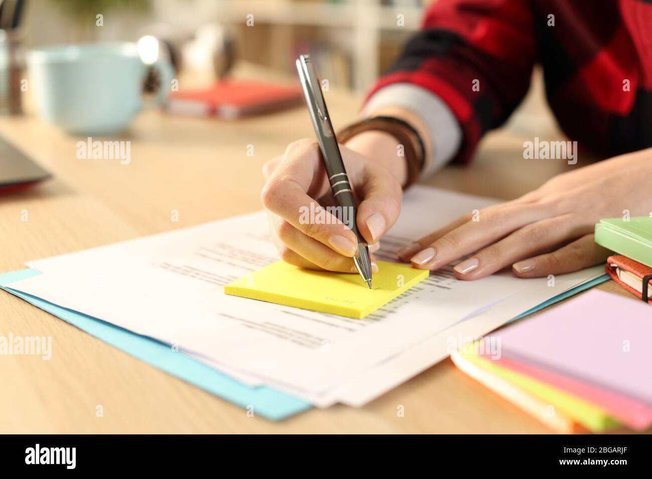 Close up of student girl hand writing on post note sitting on a desk at ...
