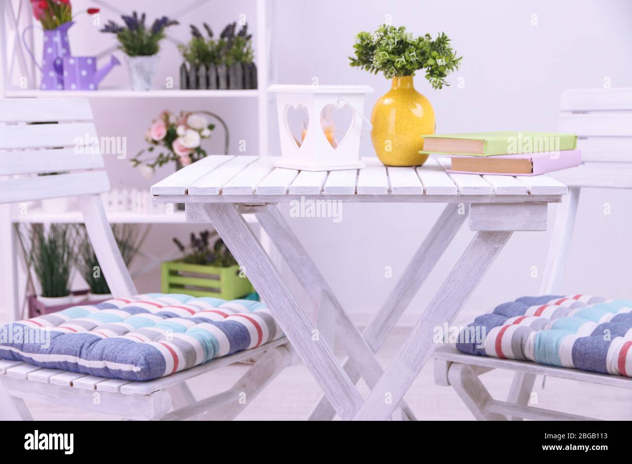 Garden chairs and table with flowers on shelves on white background ...