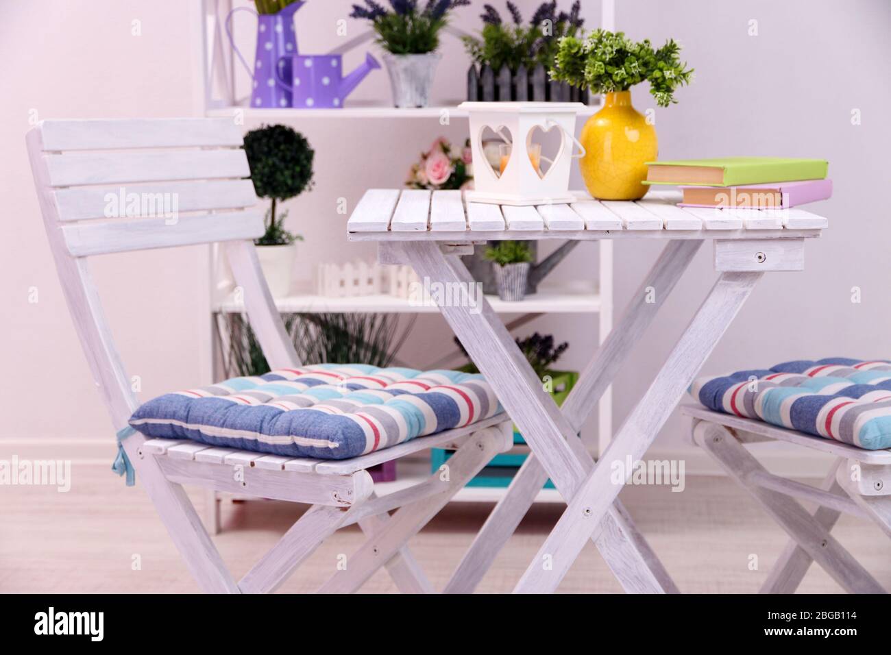 Garden chairs and table with flowers on shelves on white background ...