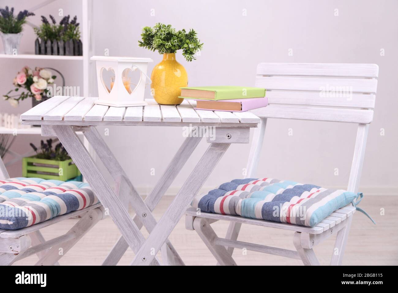 Garden chairs and table with flowers on shelves on white background ...