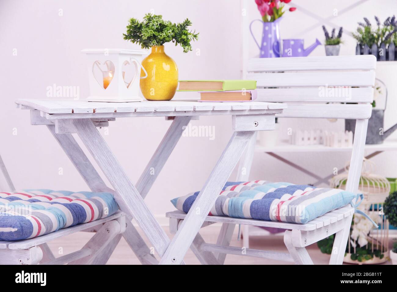 Garden chairs and table with flowers on shelves on white background ...