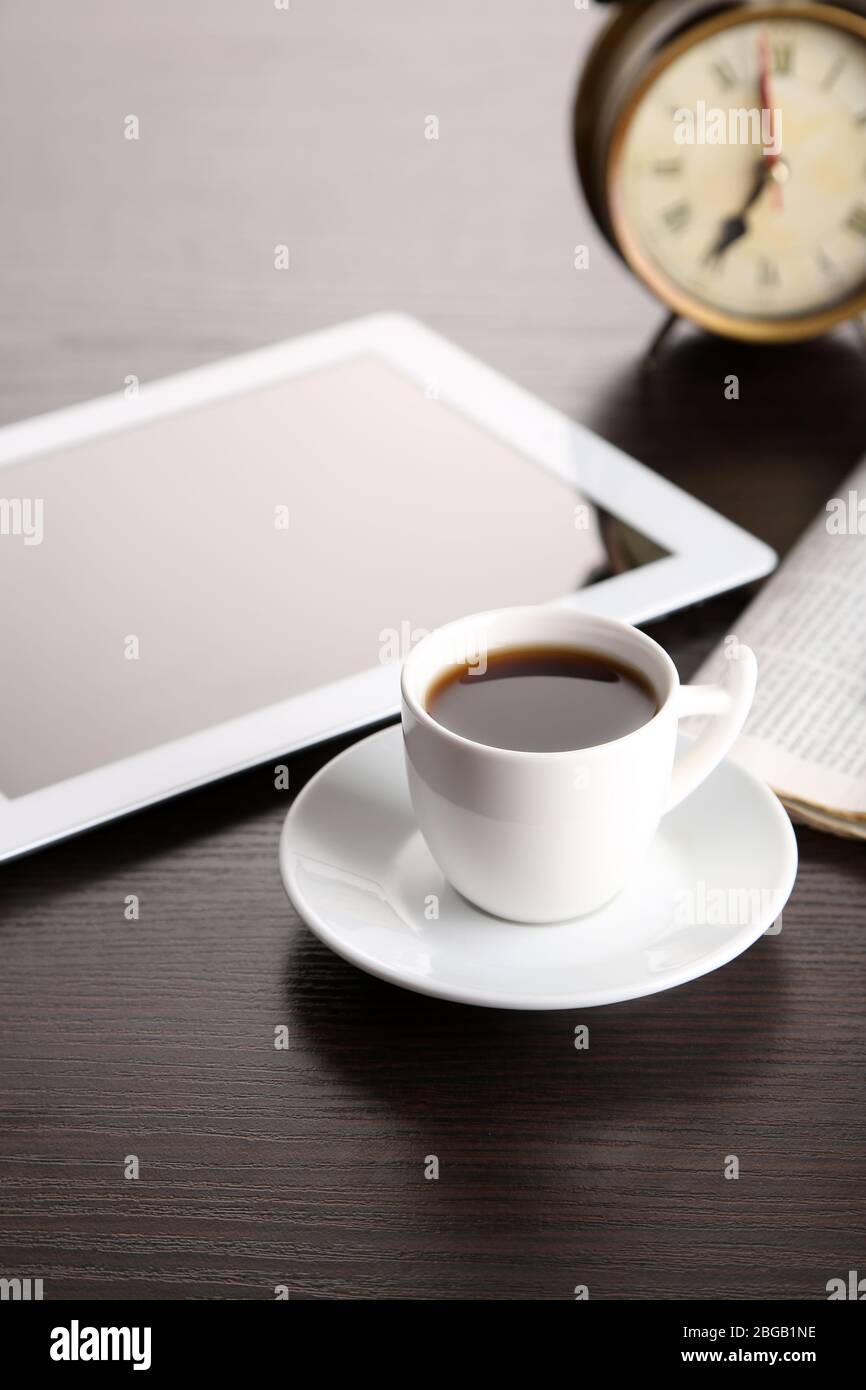 Tablet, newspaper, cup of coffee and alarm clock on wooden table Stock ...
