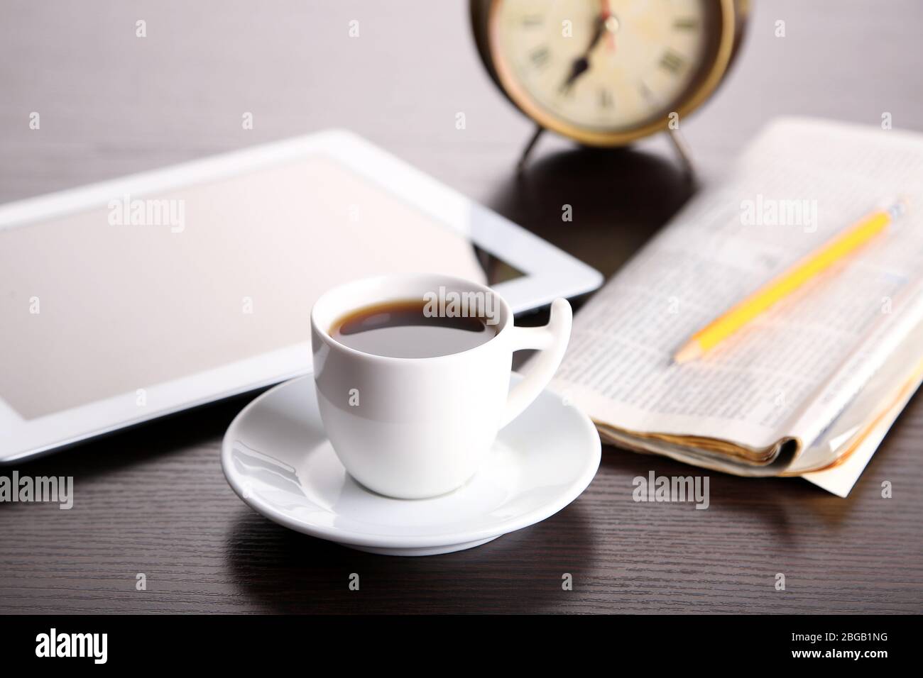 Tablet, newspaper, cup of coffee and alarm clock on wooden table Stock ...