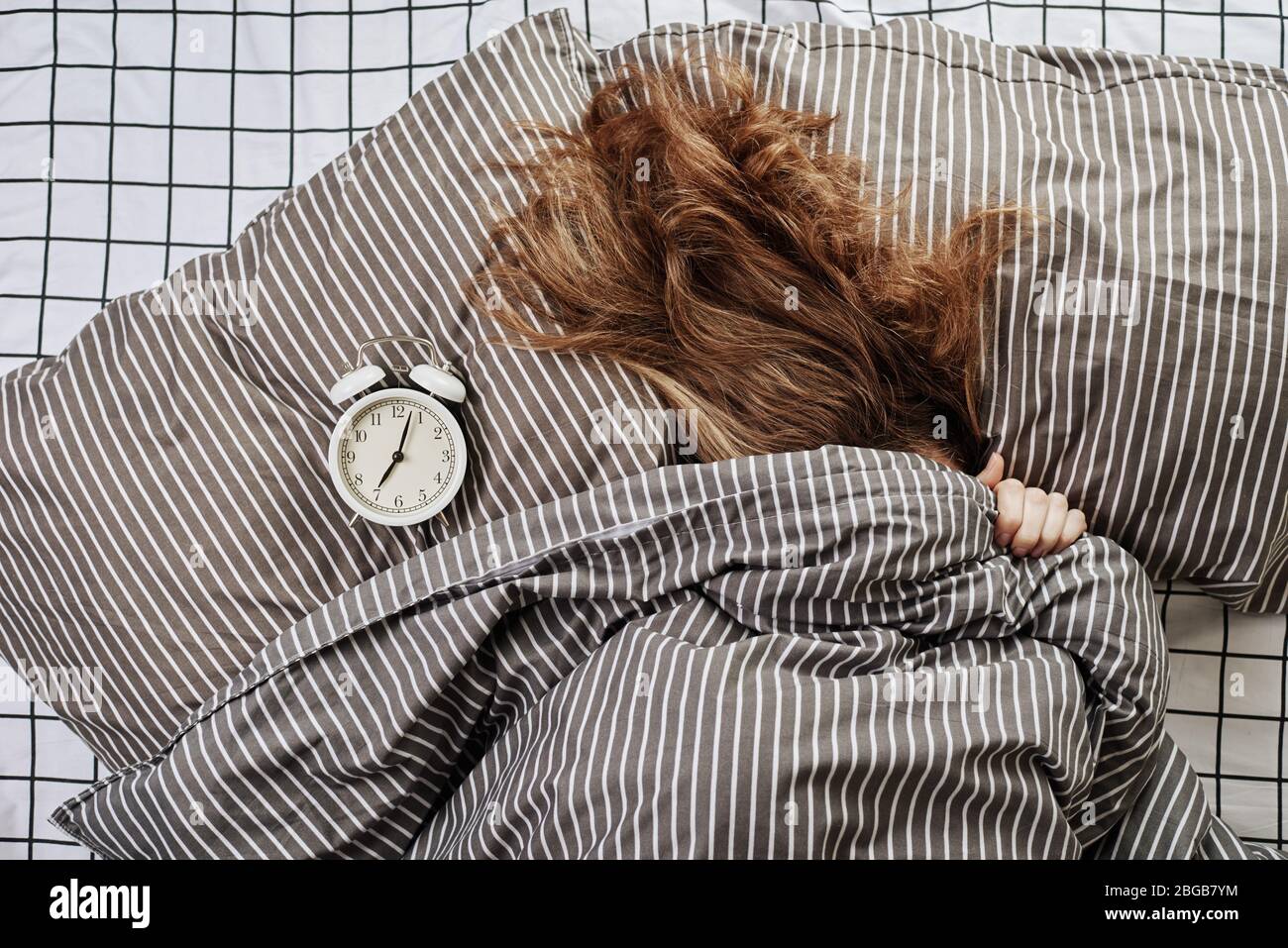 Sleeping woman covered under blanket in the bed and vintage alarm clock ...